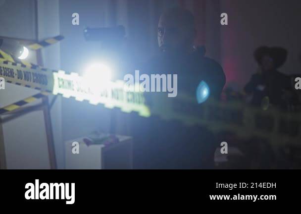 Two agents investigate a crime scene indoors, with a man aiming a gun ...