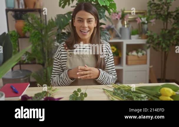 Smiling hispanic woman in apron arranging flowers at home, invoking a ...
