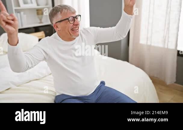 Madcap middle age grey-haired man rocking out in pyjamas, striking wild ...
