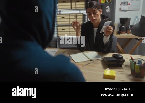 A woman investigator examines evidence while questioning a hooded ...