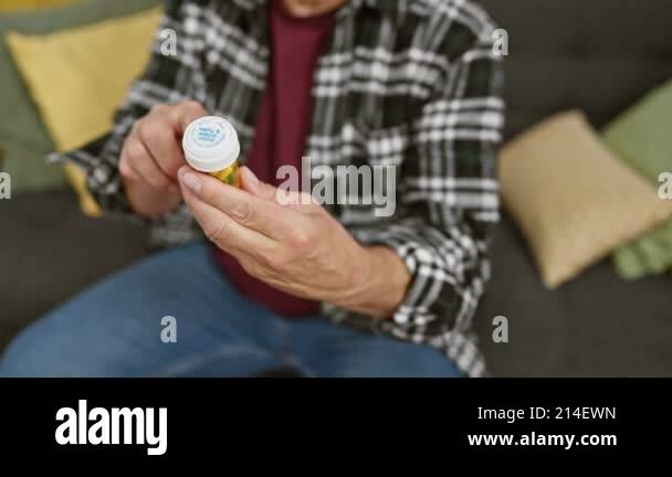 A middle-aged man examines a prescription bottle in a cozy living room ...