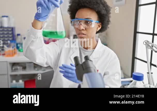 African american female scientist examining green liquid in flask at ...