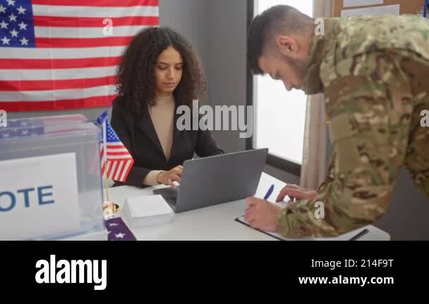 A woman assists a uniformed soldier with paperwork against a backdrop ...
