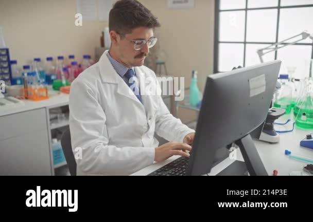 A male scientist uses a computer in a laboratory, exhibiting focus and ...