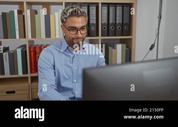 Young man with glasses working in an office with shelves of books and ...