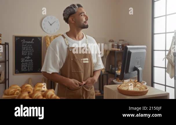 Young man standing behind the counter in a bakery shop with pastries in ...