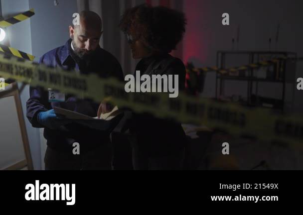 A man and woman investigating a crime scene indoors, examining evidence ...