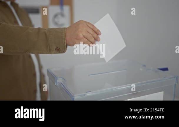 A young hispanic man casts a ballot in an indoor voting station ...