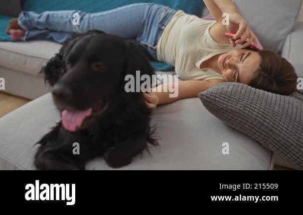 A young woman relaxing with her black labrador dog on a sofa while ...