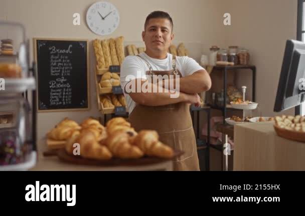 Young hispanic man in a bakery shop wearing a brown apron, standing ...