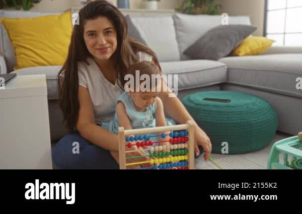 Mother playing with toddler daughter in living room using colorful abacus, surrounded by cozy ...