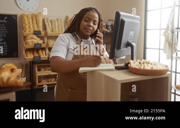 Woman working in a bakery, talking on the phone while taking notes ...