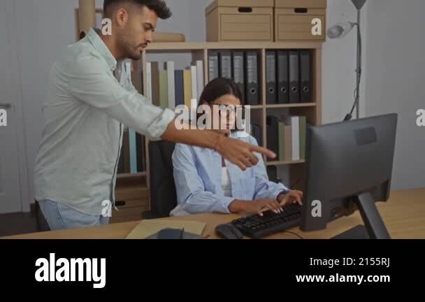 Man standing over woman working on computer in an office with folders ...