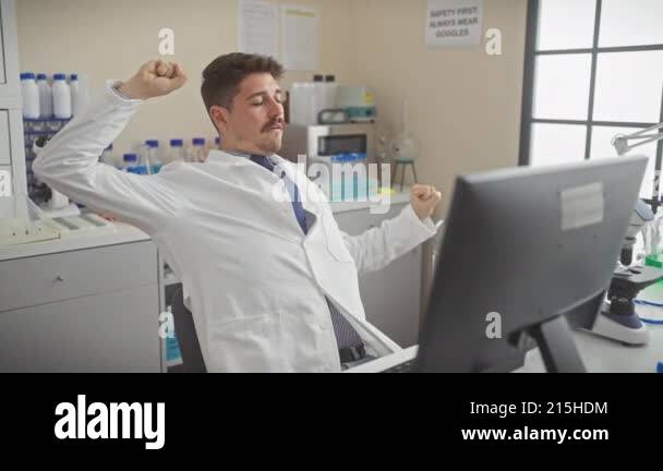 A young man in lab coat stretches during a break in a scientific ...