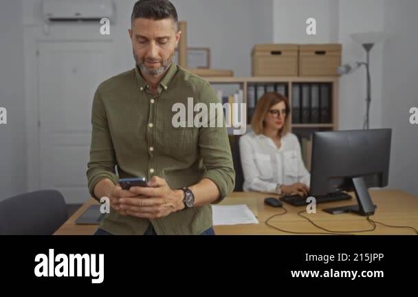 Man texting on phone while woman works on computer in modern office ...