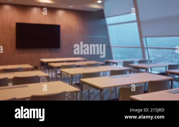 Classroom setting with rows of empty desks and chairs facing a large screen in a modern ...