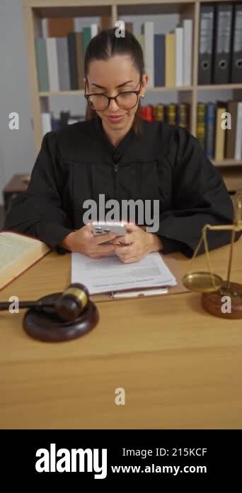 Female judge sitting at desk in courtroom, looking at smartphone, with ...