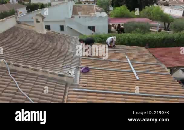 Workers on a red-tiled roof cutting and preparing mounting areas for ...