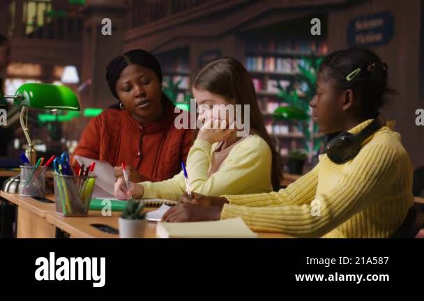African american professor mentoring diverse students in the library ...