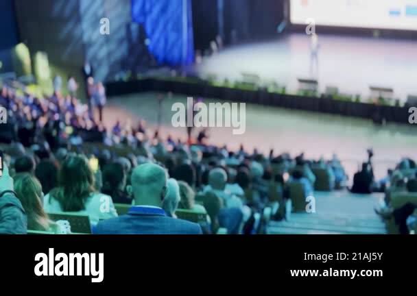 Conference setting with audience in focus and a speaker on stage ...