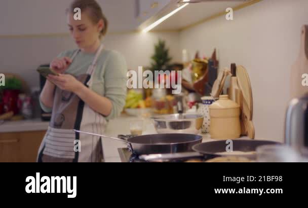 A woman leans against the counter in the kitchen, browsing social media ...