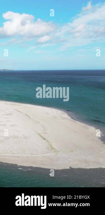 The video shows a thin strip of white sand in a blue ocean. A blue sky ...