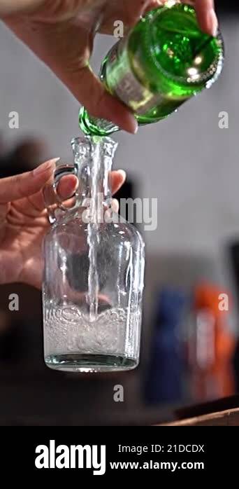 Pouring sparkling water from green bottle into glass jug, refreshing drink preparation, close-up ...