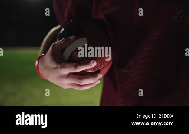 A close-up view of an American football player holding the ball under ...
