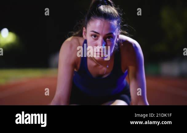 Female Runner on Athletics sprint race starting blocks on a dark ...
