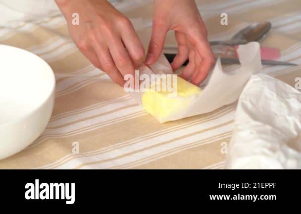 A young woman unwraps butter wrapped in parchment and cuts it into ...