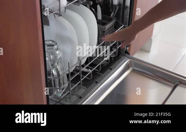 A persons hand opening a dishwasher filled with sparkling clean dishes ...