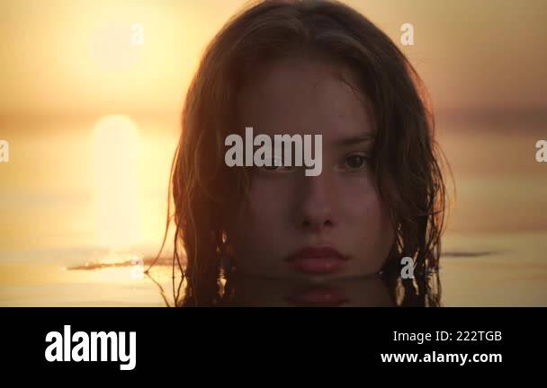 A close-up of a woman partially submerged in calm waters, her wet hair ...