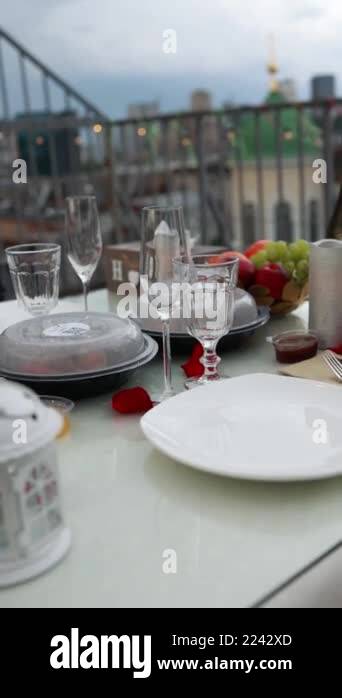 Rooftop dining table elegantly set with glassware, covered dishes, rose ...