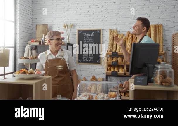 Two bakers, a woman and a man, smiling and high-fiving in a bakery shop ...