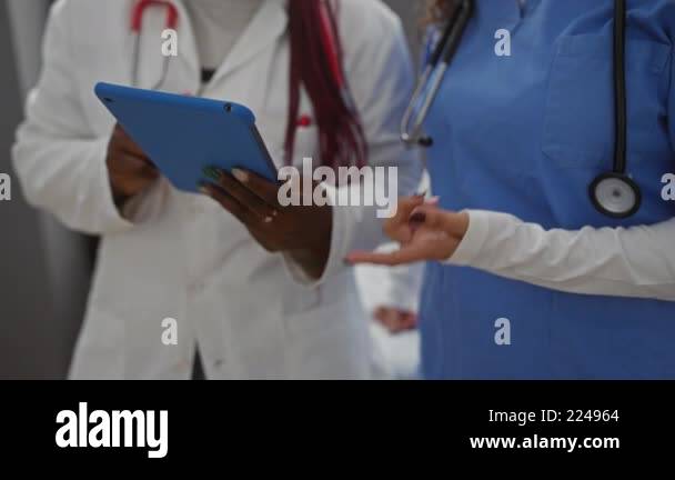 Women doctors collaborating in a hospital room, using a tablet for ...