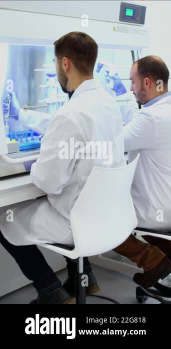 vertical Two professional scientists in white coats are sitting at a ...