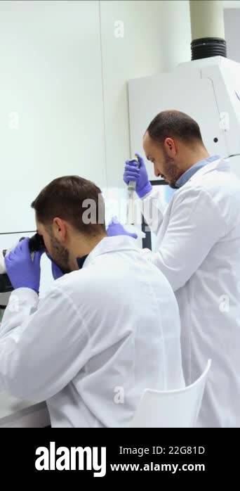 vertical Scientists in white lab coats and purple gloves conducting ...
