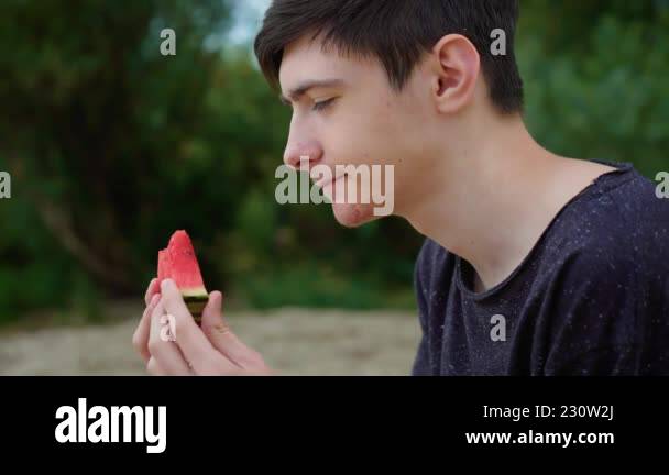 Boy teenager eating watermelon, enjoying its juicy taste with focused ...