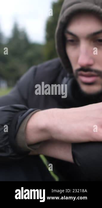 Alone man smoking thoughtfully leaning against a tree in the park ...