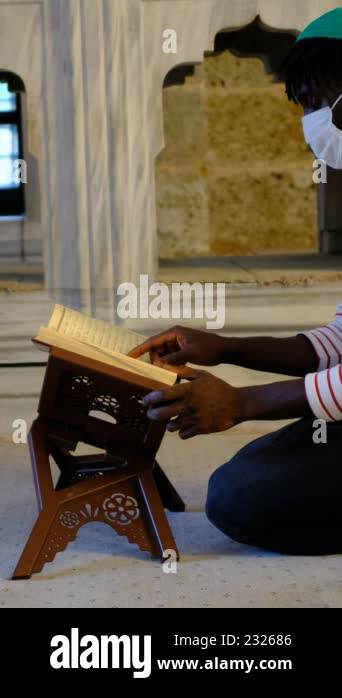 A black muslim man with a mask on his face is reading the Koran in a ...