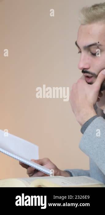 Young man reading a book at his desk indoors, carefully examining the ...