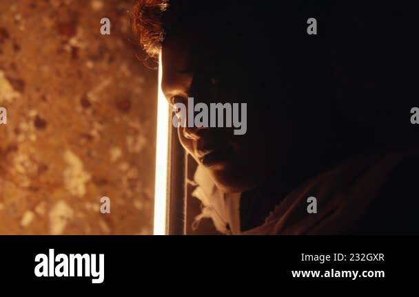 A close-up of a person's face partially illuminated by a bright light ...