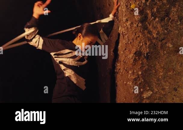 A dancer performing in a dimly lit cave, with white ribbons wrapped ...