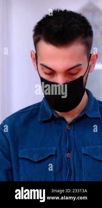 Close-up shot of young man with black mask on his face praying in ...