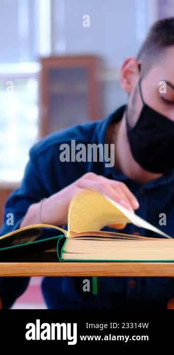 Muslim teenager with black mask on his face changing pages of quran ...