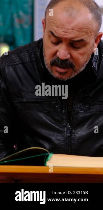 Close-up of an old man sitting in a mosque reading the Quran standing ...