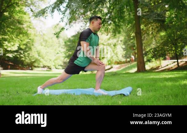 Young sportsman performs gymnastics on mat in urban city park. Sporty Japanese male is ...
