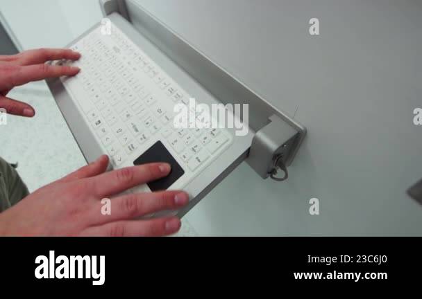 Close-up of hands typing on a clean white keyboard mounted to a wall ...