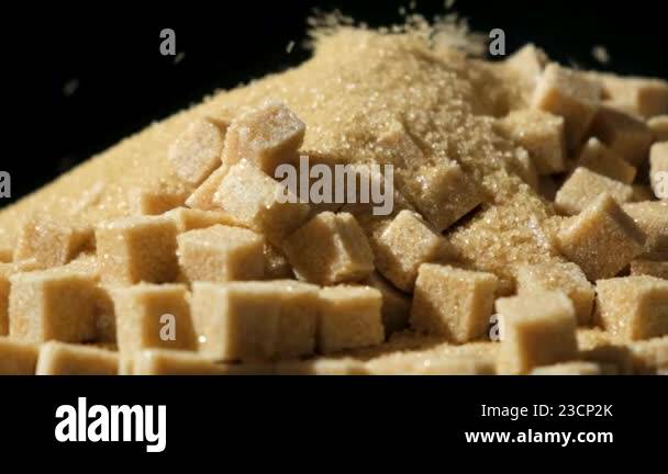 Cane sugar cubes falling into a pile of crystalline brown sugar, slow ...