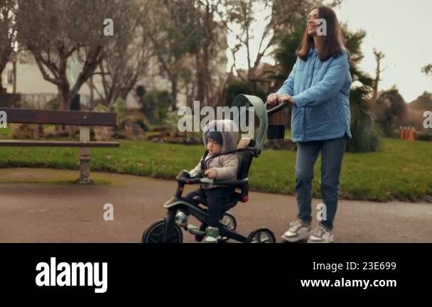 Close-up of a mother carrying a stroller, a tricycle with a baby in an ...